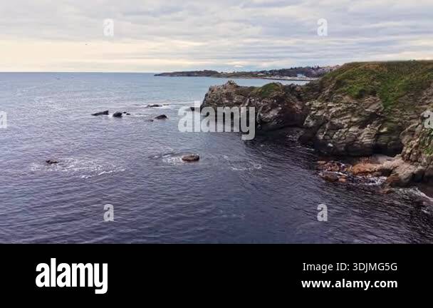 An aerial view showcases rocky coastal cliffs meeting the tranquil ...