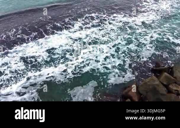 An aerial view captures waves rolling and crashing against rocky shores ...