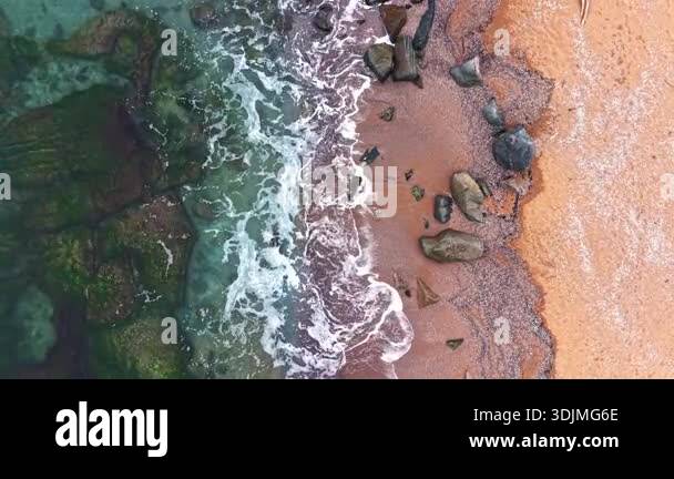 Aerial view captures waves rolling onto a sandy beach, with rocks ...