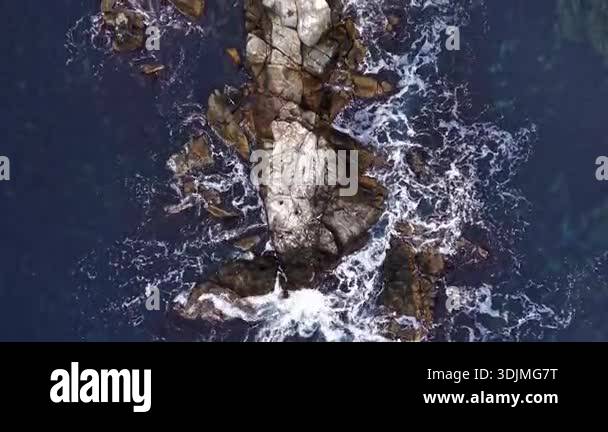 Aerial view of large coastal rocks surrounded by crashing waves. The ...