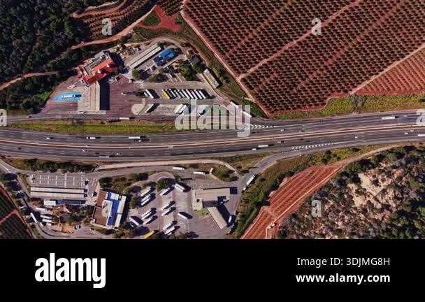 Cars drive on a highway near a service area and vineyards. Trucks are ...