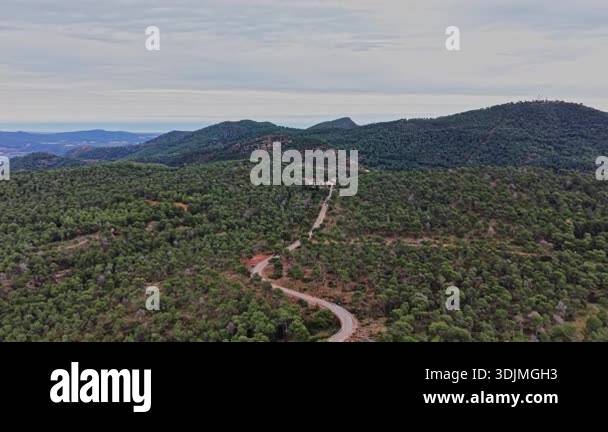 A winding road cuts through the green hills of Spain. Trees surround ...