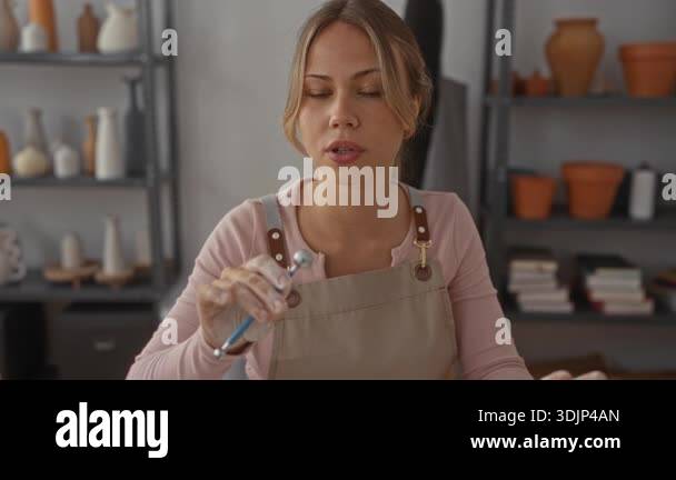 Potter woman holds clay modeling tool with clay covered hand in pottery ...