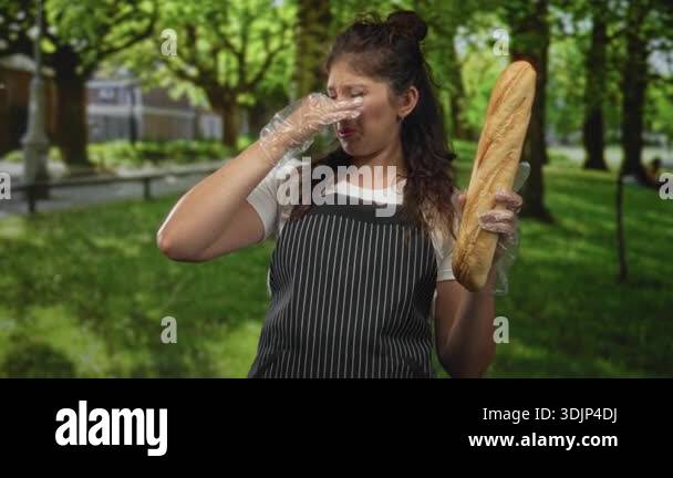 Woman pinches nose while holding a long baguette, wearing a striped ...