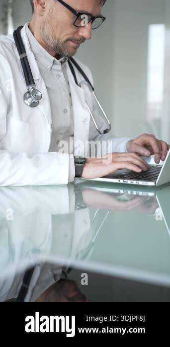 Doctor wearing a lab coat and stethoscope, typing on a modern laptop at ...
