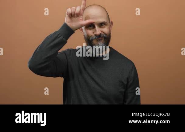 Man gesturing loser sign isolated against brown wall with bald head and ...