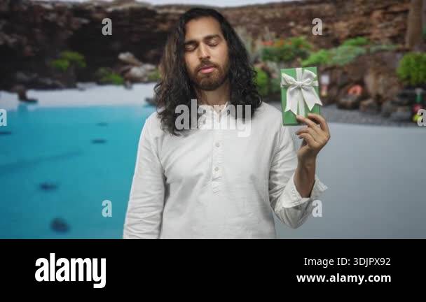 Man holding green gift with raised hand by pool outdoors near turquoise ...