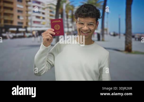 Man holds greek passport up on street while smiling broadly under palm ...