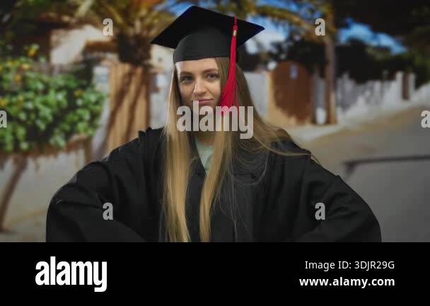 Woman wearing graduation cap and gown, standing on a city street ...