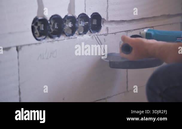Male construction worker cutting groove chase for electric cables in ...