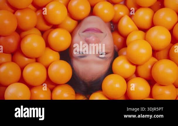 A cheerful top-down portrait of a man lying in a sea of orange balls ...