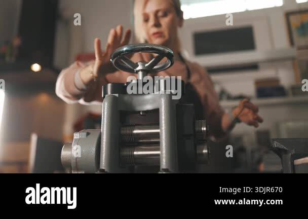 Artisan woman passing a thin metal wire through a goldsmith rolling ...