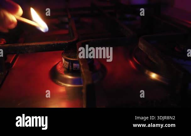 Hand uses a lit match to ignite two gas stove burners in sequence ...