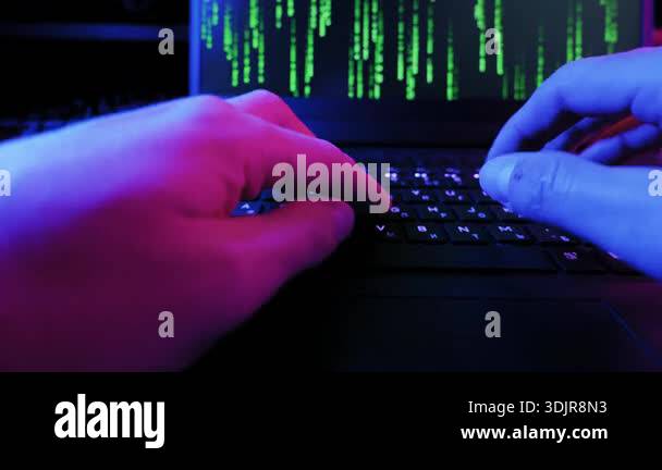 Hackers hands type rapidly on a laptop keyboard with green code on the ...