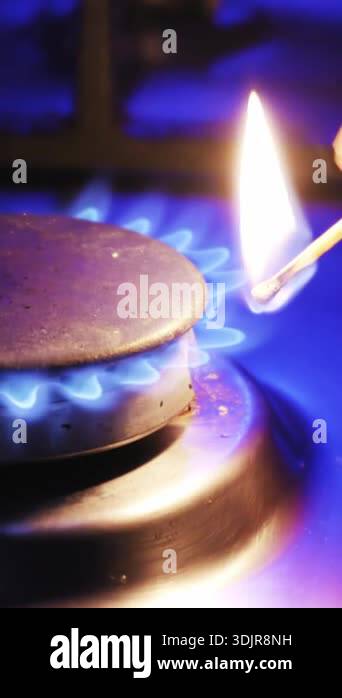 Hand holds a lit match to ignite a gas stove burner, which erupts in a ...