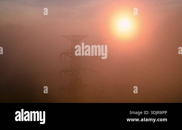 A high-voltage power line tower stands tall amidst a vibrant orange and ...