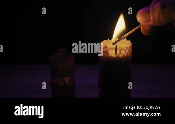 A hand lights a textured beeswax candle using a burning match against a ...