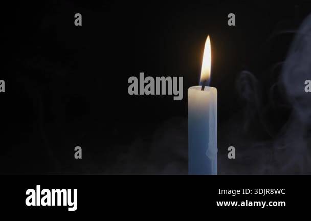 A single blue wax candle burns brightly with white smoke swirling ...