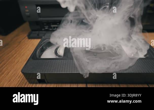 Black VHS cassette sits on wooden table emitting thick white smoke near ...