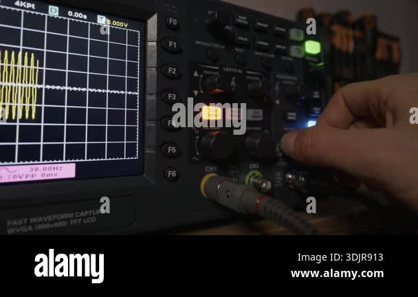 An engineer adjusts a digital oscilloscope, changing the scale of a ...