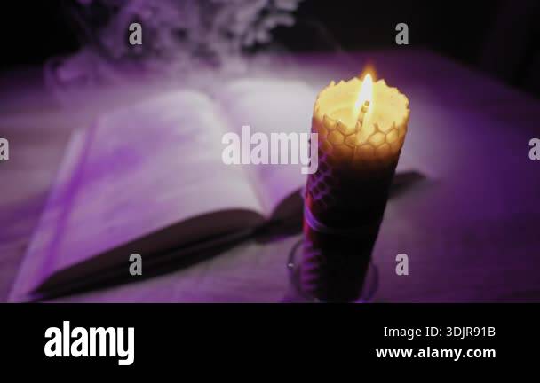 Textured beeswax candle burning near open book with swirling purple ...