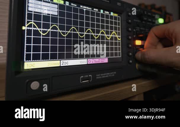An engineers hand adjusts the controls on a digital oscilloscope ...