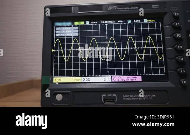 A digital oscilloscope screen displays a yellow sine wave as the camera ...