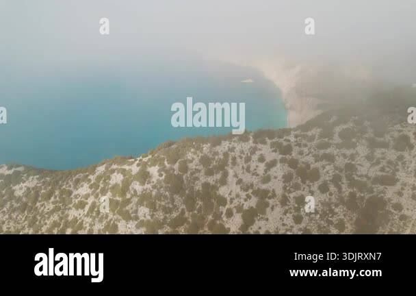 Flight through mist over blue sea and coastal hills in Kefalonia Island ...