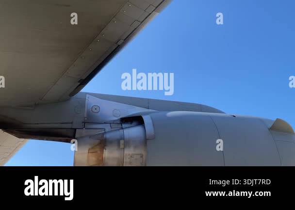A powerful jet engine sits beneath the wing root of a large airplane ...