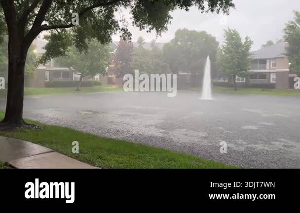 Strong rain pours down on a pond with a water fountain in the middle ...