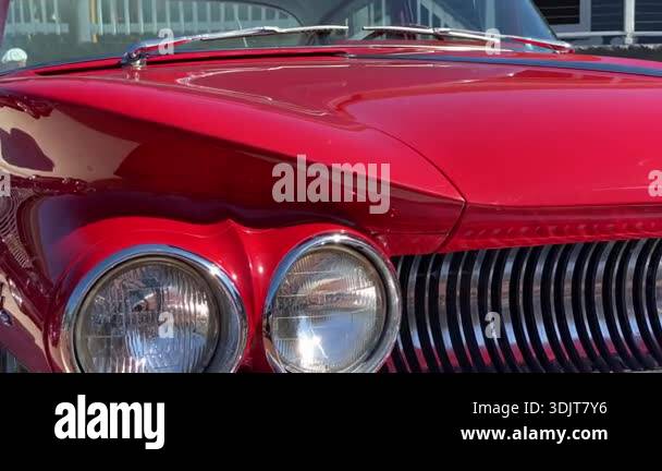 Bright red classic car front shows two round headlights, chrome trim ...