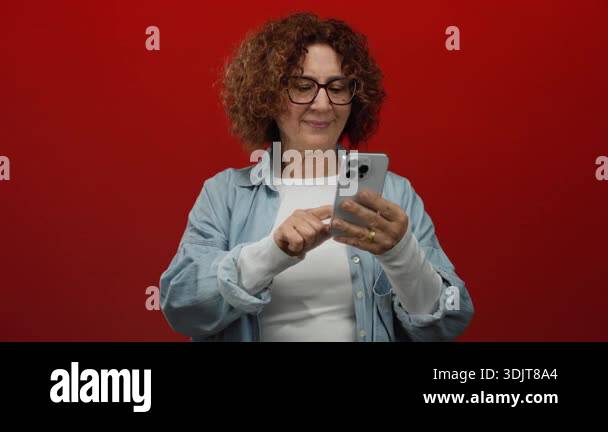 Hispanic woman gestures ok while using smartphone against vibrant red ...