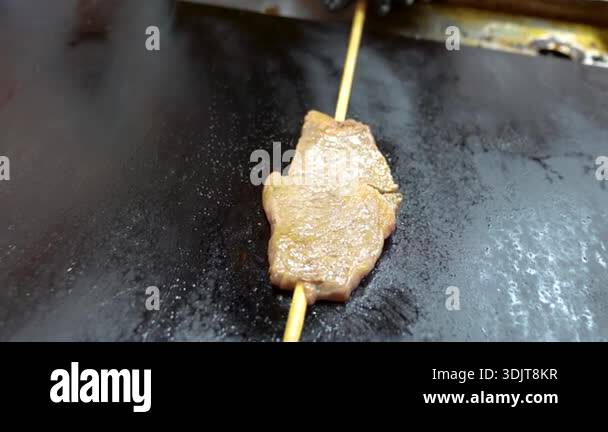 Wagyu steak is grilled on a skewer, revealing the juicy texture and ...