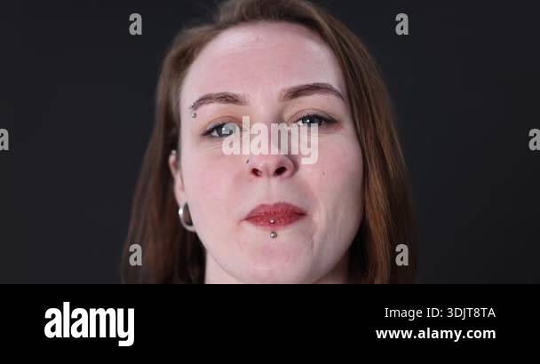 Young woman with piercings, tattoos and stylish clothes posing on dark ...