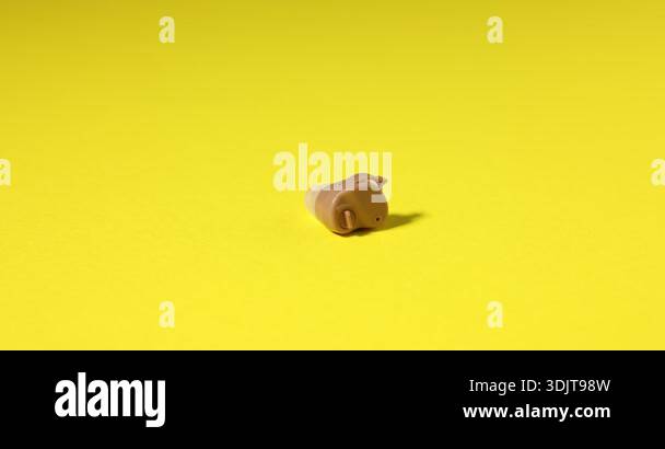 One modern hearing aid on yellow background, closeup. Camera moving ...