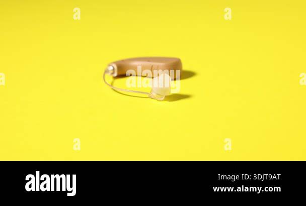 One modern hearing aid on yellow background, closeup. Camera moving ...