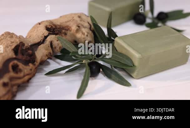 Handmade soap bars, olives, snag and green leaves on white wooden table ...