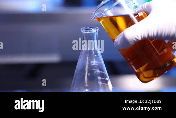 Woman pouring orange liquid from glass beaker into flask in laboratory ...