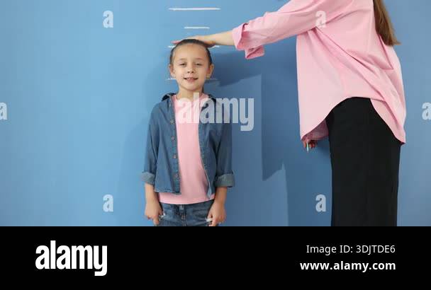 Woman measuring her daughter's height near blue wall indoors, closeup ...