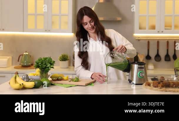 Smiling woman pouring delicious smoothie from blender into glass at ...