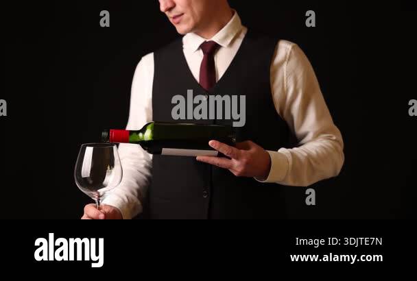 Professional sommelier pouring red wine into glass on black background ...