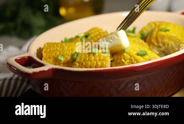 Pieces of boiled corn cobs with green onion and butter in baking dish ...