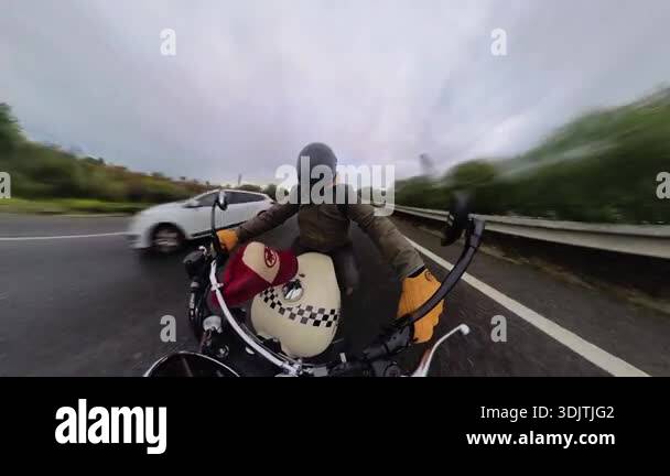 4k shot of a man riding a scrambler-type motorcycle on the road while ...