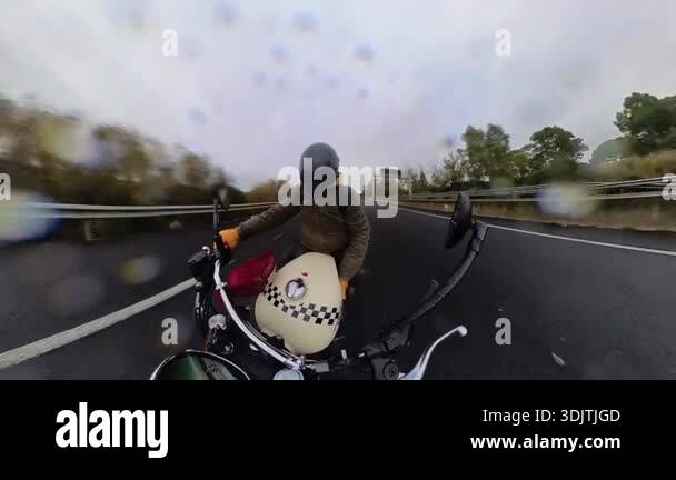 4k shot of a man riding a scrambler-type motorcycle on the road while ...
