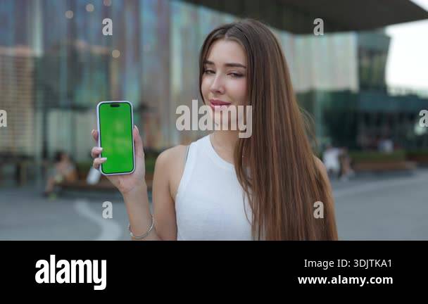Portrait of young woman presents app on chroma key smartphone screen in ...
