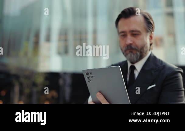 Portrait of grey bearded businessman reads news on digital tablet on ...