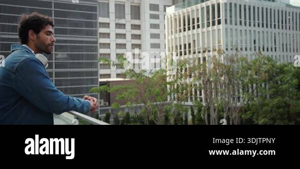 Portrait of Hispanic man with earphones leans onto railing in downtown ...