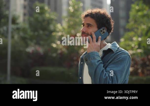 Portrait of Hispanic man talks on smartphone and walks along street ...