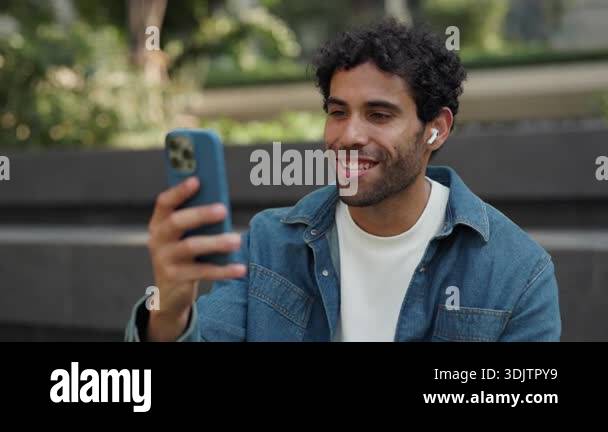 Portrait of young Hispanic man answers video call on smartphone in ...