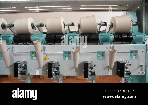 Automated textile machinery rewinding cotton threads onto bobbins in a ...